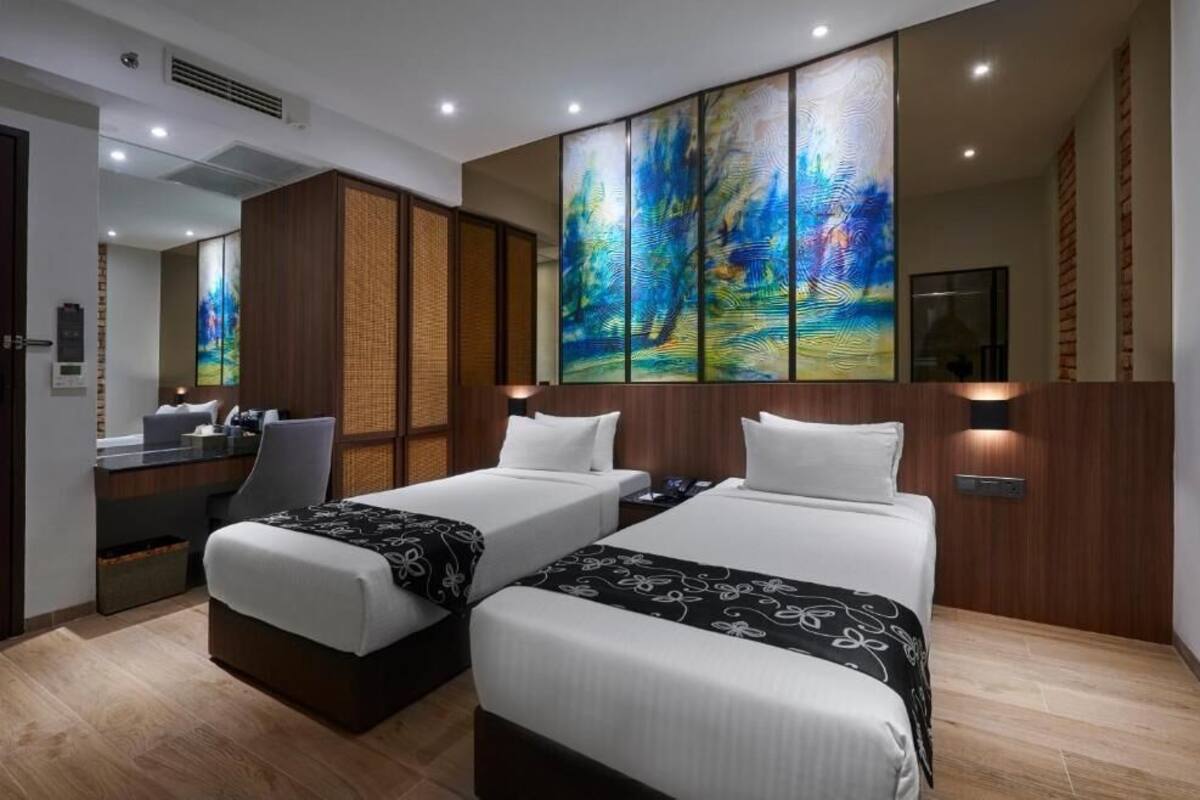 Quarto de hotel com duas camas, uma escrivaninha e um grande quadro abstrato na parede.