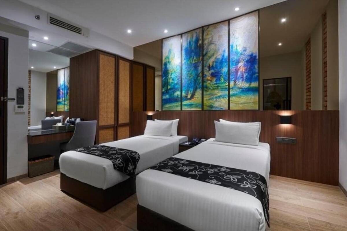 Quarto de hotel com duas camas, uma escrivaninha e uma grande pintura abstrata na parede.