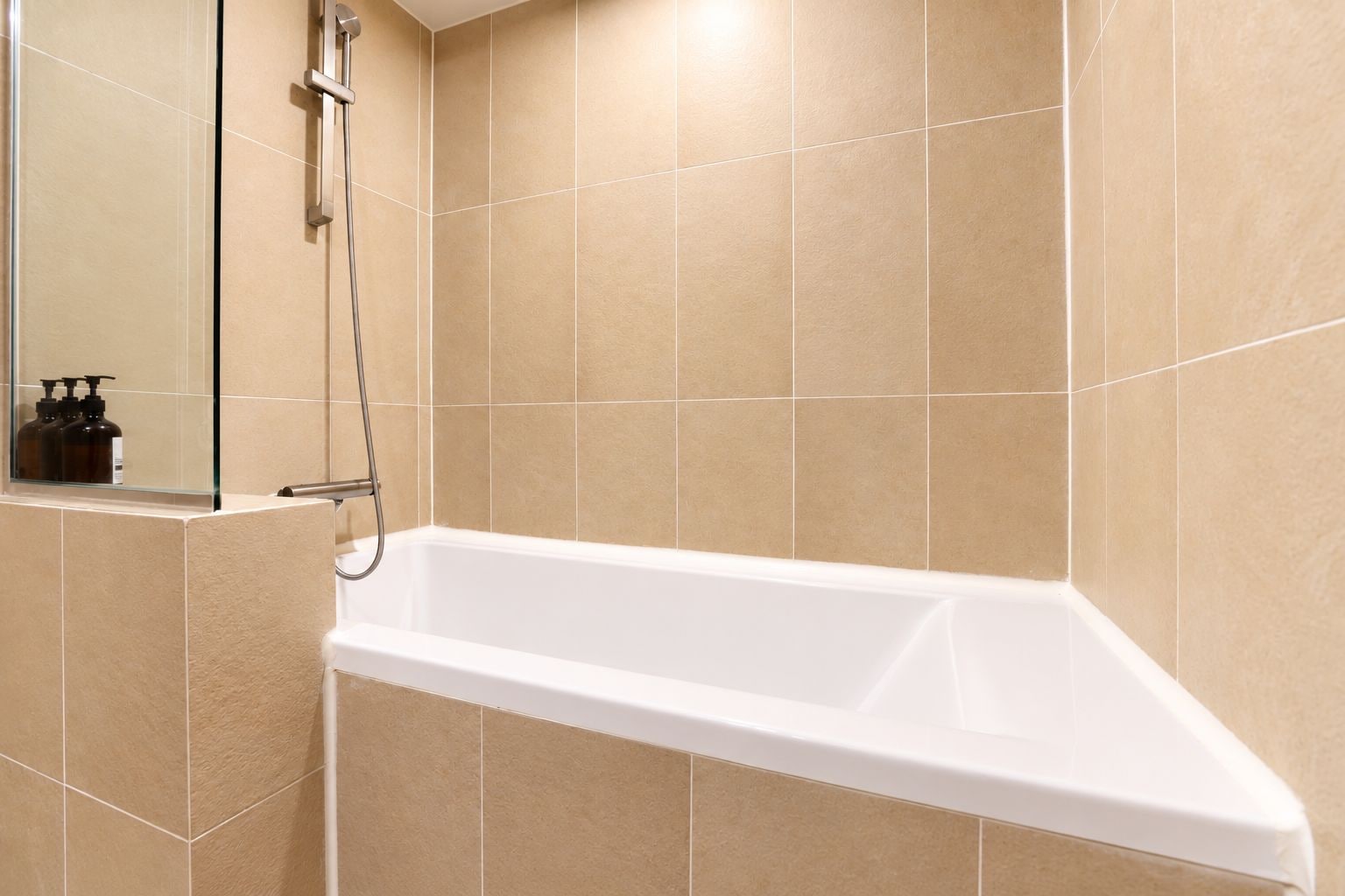 Casa de banho de canto com banheira branca, azulejos bege e cabine de duche em vidro.