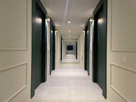Corredor de hotel comprido e estreito, com portas em ambos os lados, iluminação embutida e piso de azulejos.