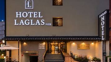 Entrada de hotel com uma placa indicando 'HOTEL LAGLAS' e uma escadaria que leva ao saguão.