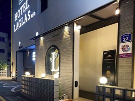 Entrada de um hotel com design moderno, exibindo uma placa grande com a inscrição 'HOTEL LAGLAS', uma área de estacionamento e uma placa com o prêmio 'KCIA'.