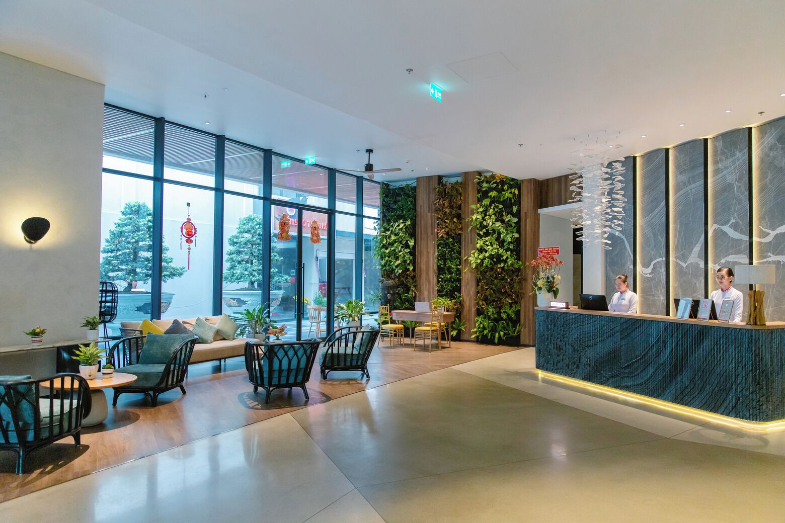 Um hall de hotel moderno com balcão de recepção, área de estar com sofás e poltronas, janelas amplas e plantas em vasos.