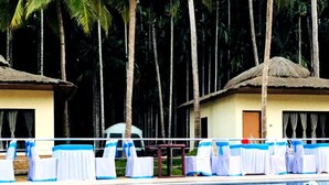 Uma piscina com espreguiçadeiras e um flutuador, cercada por palmeiras e palafitas com telhados de palha.