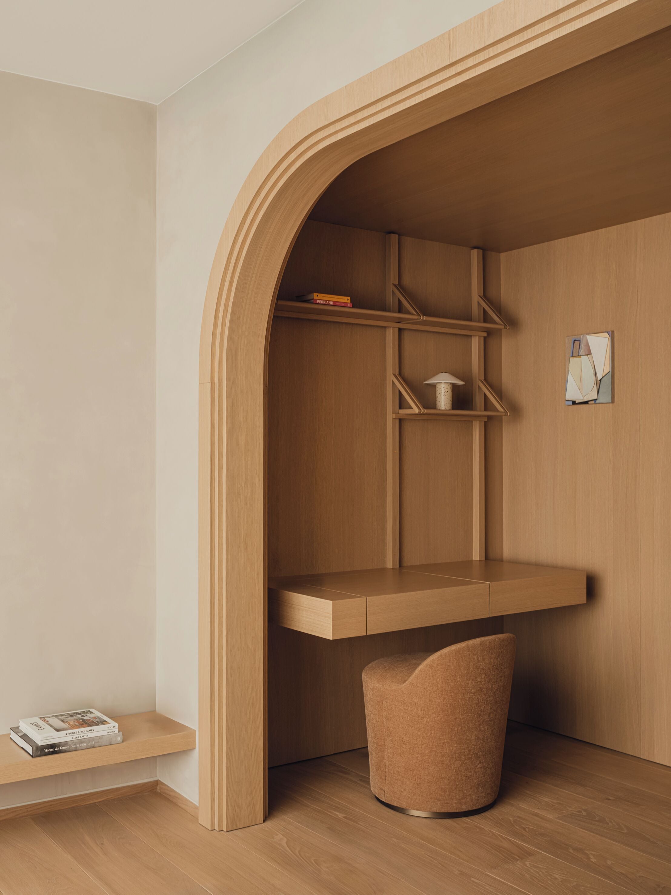 Quarto moderno e minimalista com estantes de madeira embutidas, um pequeno espaço de estar e uma luminária fixada na parede.