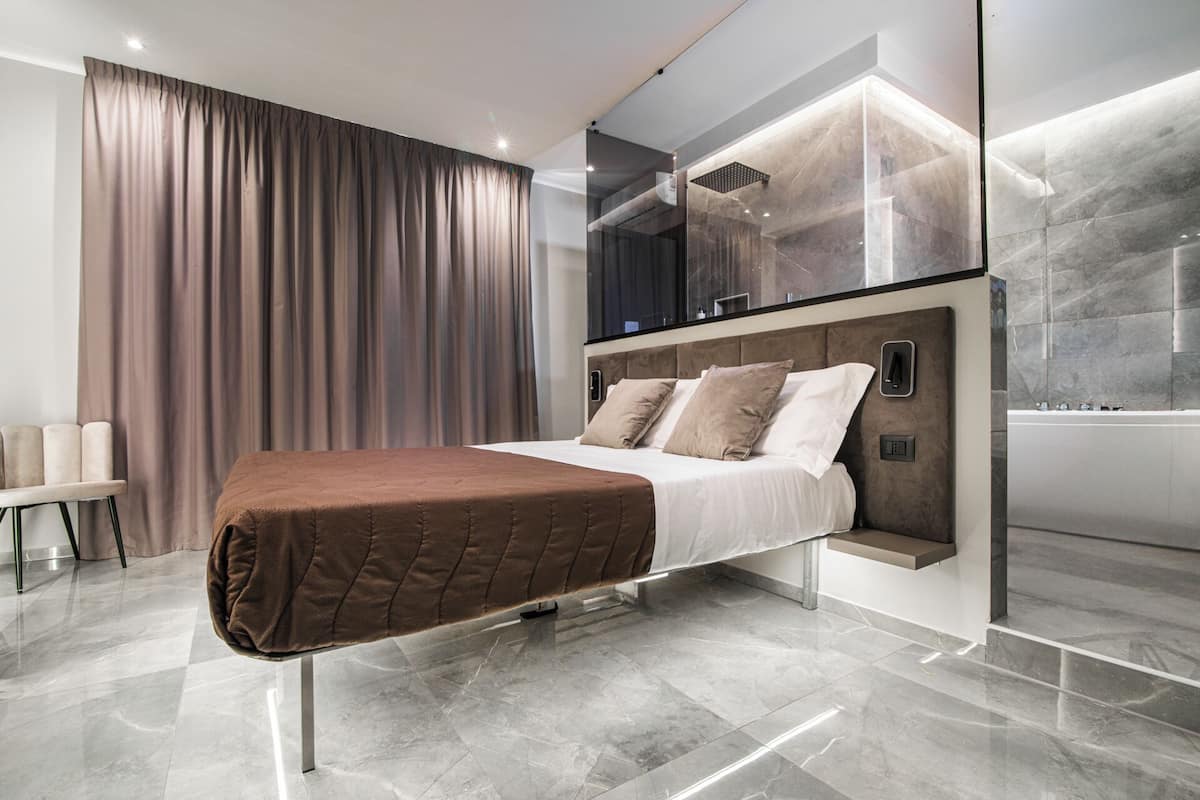 Quarto moderno com cama, mesa de cabeceira e uma janela grande com cortinas.