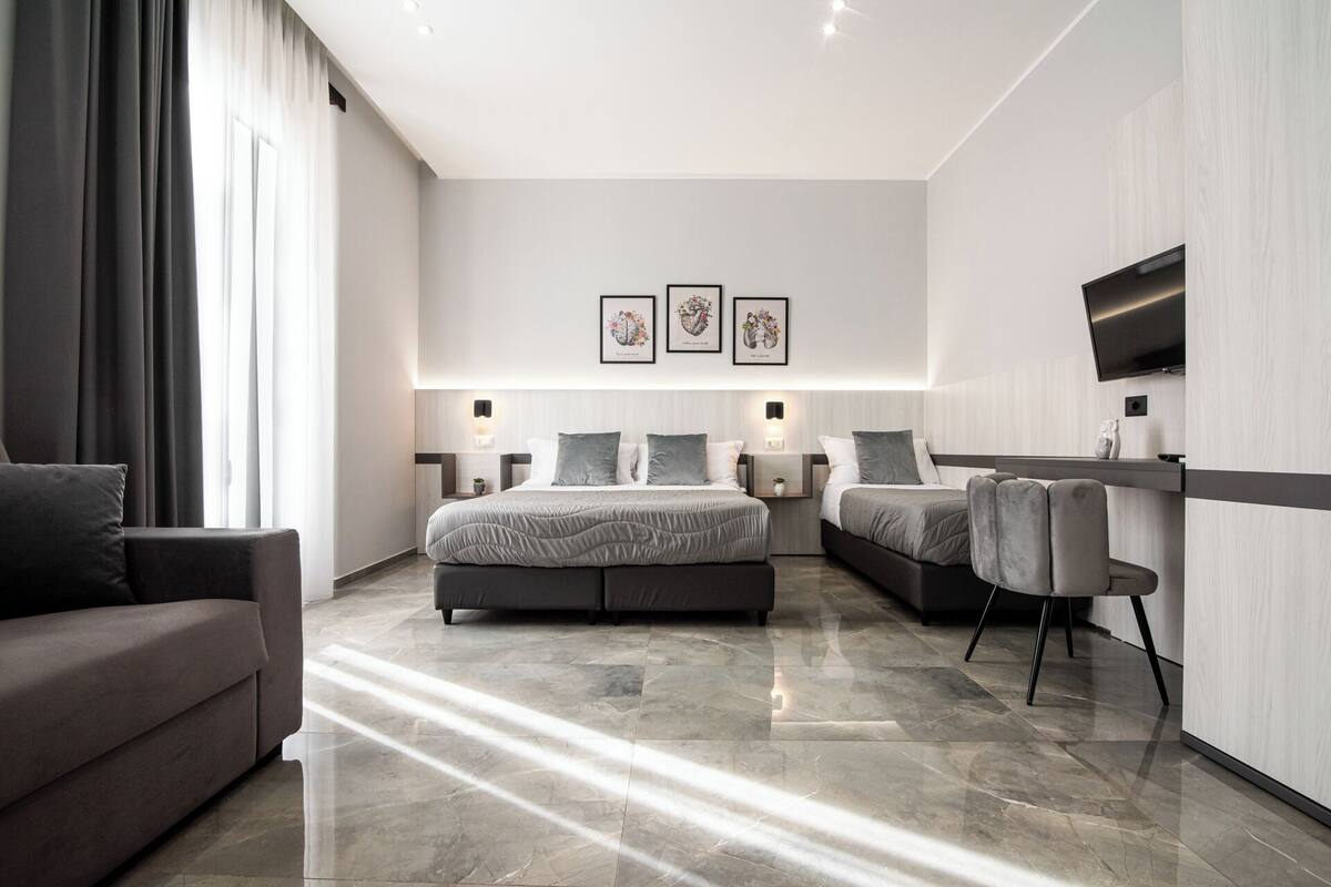 Quarto de hotel moderno com uma cama grande, um sofá, uma escrivaninha com cadeira e uma televisão de tela plana fixada na parede.