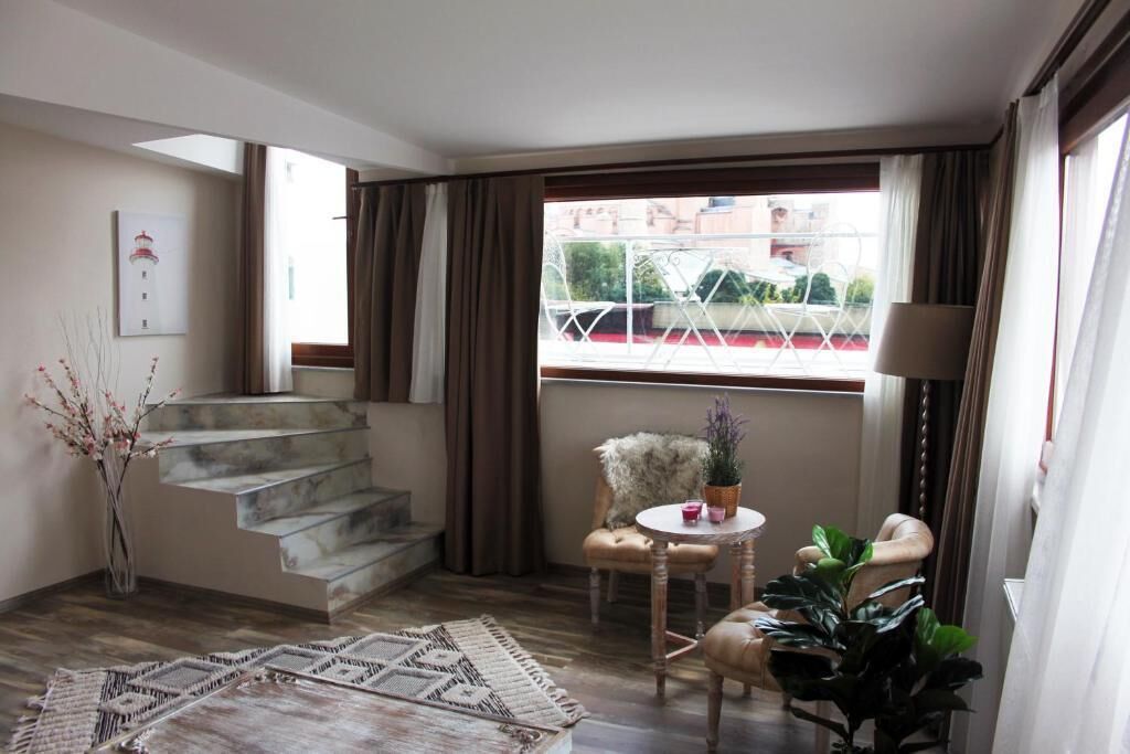 Uma sala de estar moderna com escada, área de jantar com mesa e cadeiras, e uma janela grande com cortinas.