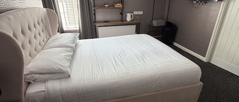 Quarto de hotel com uma cama grande, televisão na parede e uma janela com cortinas.