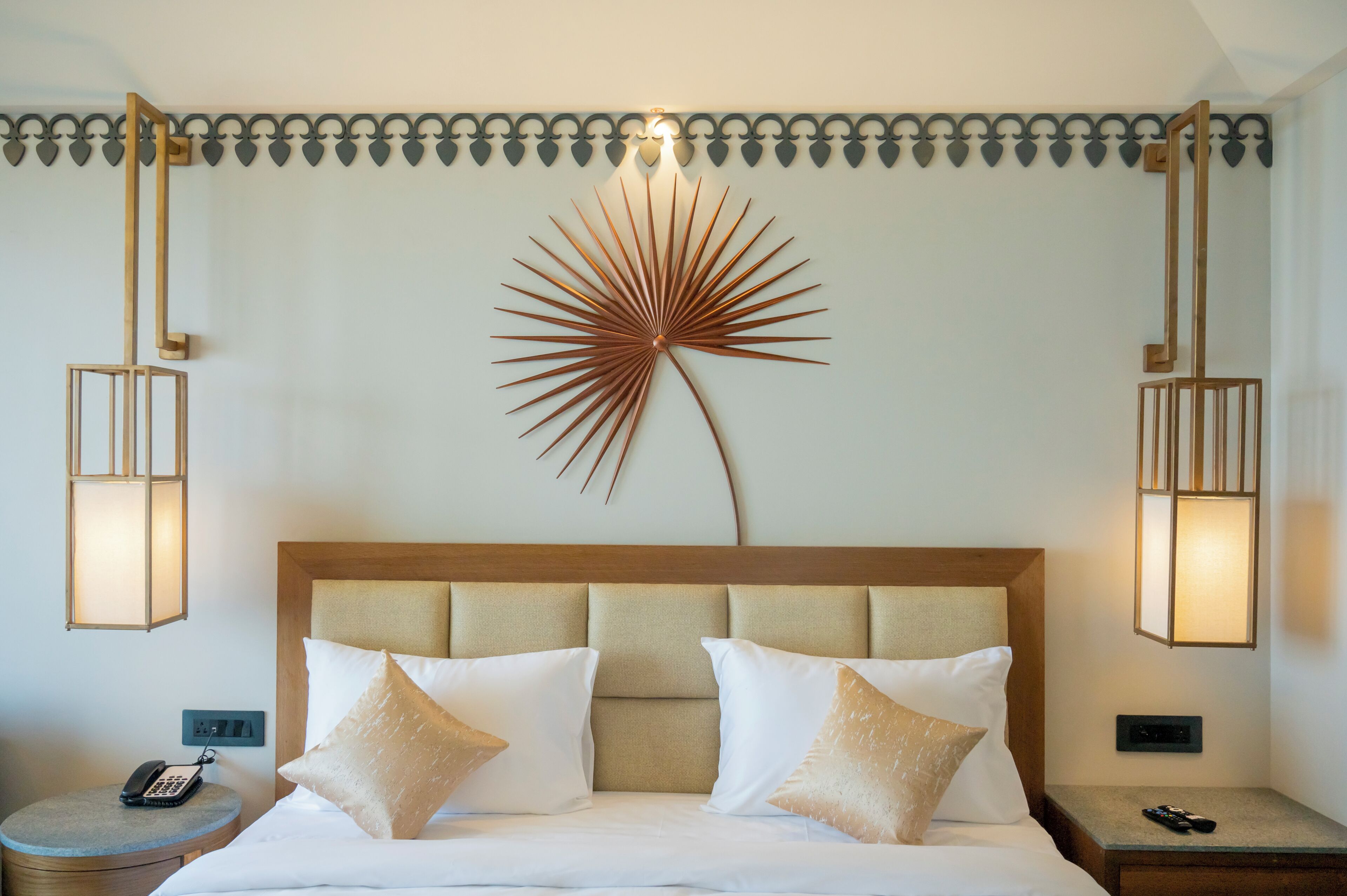 Quarto de hotel com uma cama grande, duas mesas de cabeceira, luminária fixada na parede e um objeto decorativo na parede.