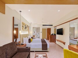 Quarto de hotel moderno com uma cama grande, um sofá, uma televisão e uma escrivaninha.