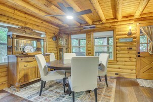 Interior de uma cabana de madeira com uma mesa de jantar, cadeiras, um relógio e um letreiro com a frase 'THE LAKE'.