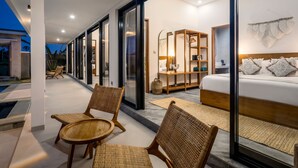 Quarto de hotel moderno com uma cama grande, uma mesa de cabeceira de madeira e uma varanda envidraçada com móveis de vime.