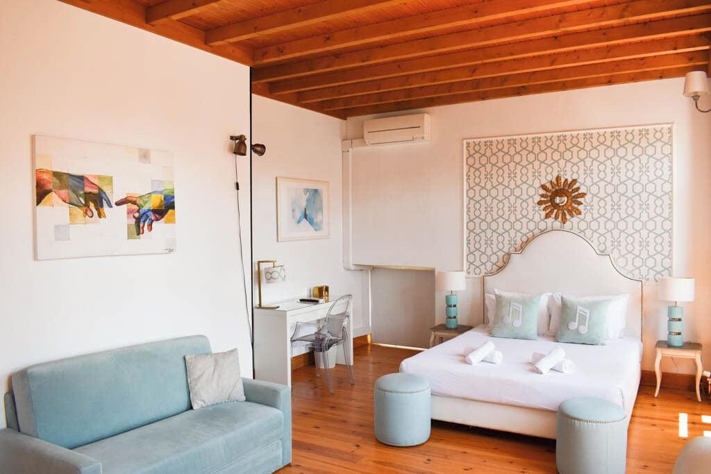 Quarto com cama, escrivaninha, cadeira e obras de arte nas paredes.