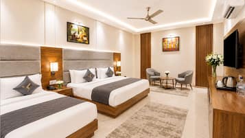 Quarto de hotel com duas camas, uma escrivaninha, uma cadeira, uma televisão e obras de arte nas paredes.