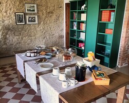 Disposição para o café da manhã com uma mesa coberta por uma toalha de padrão, diversos alimentos e uma cafeteira.