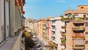 Uma fileira de edifícios altos com varandas, céu claro e carros estacionados na rua.