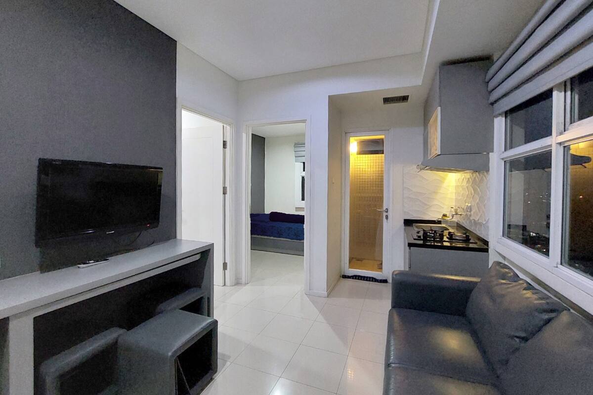 Uma sala de estar moderna com televisão de tela plana, um sofá e uma área de cozinha com fogão e pia.