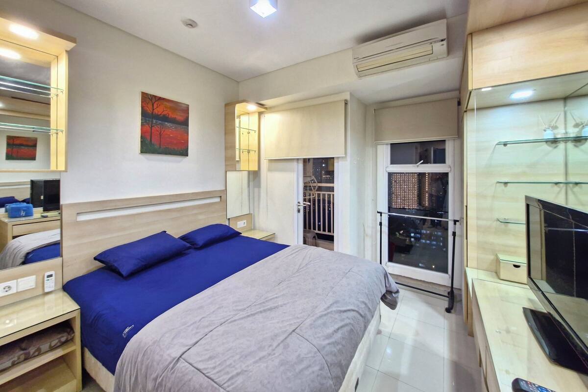 Quarto de hotel com cama, televisão, escrivaninha, espelho e janela com vista para a cidade.