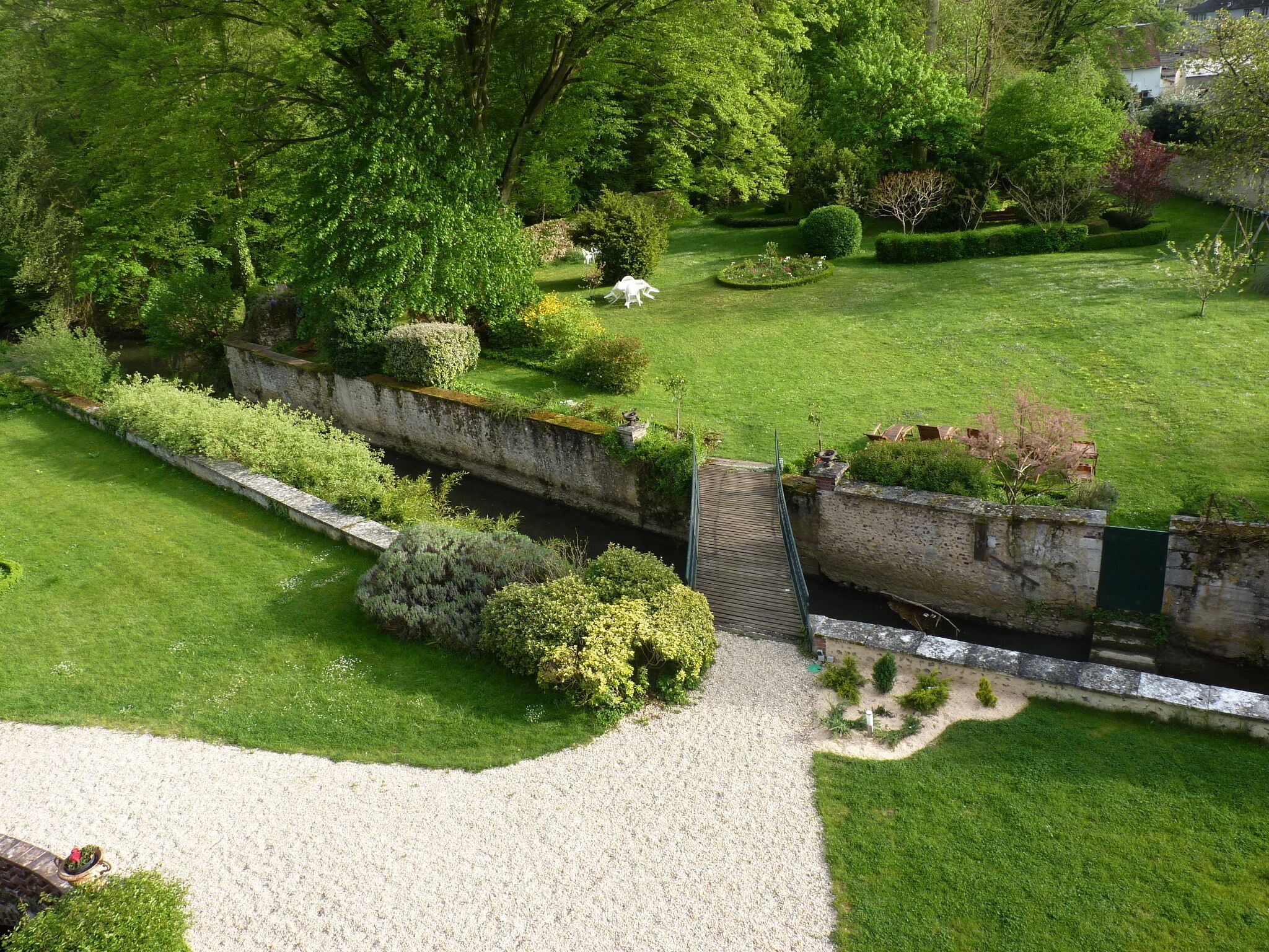 Um jardim bem cuidado com um caminho de cascalho que leva a uma ponte de madeira sobre um espelho de água.