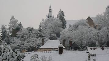 Paisagem coberta de neve com o campanário de uma igreja ao fundo, rodeada por árvores e edifícios.