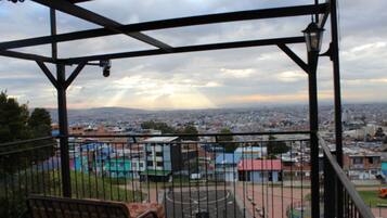 Varanda com guarda-corrimão de metal vista para a paisagem urbana com edifícios e um parquinho.