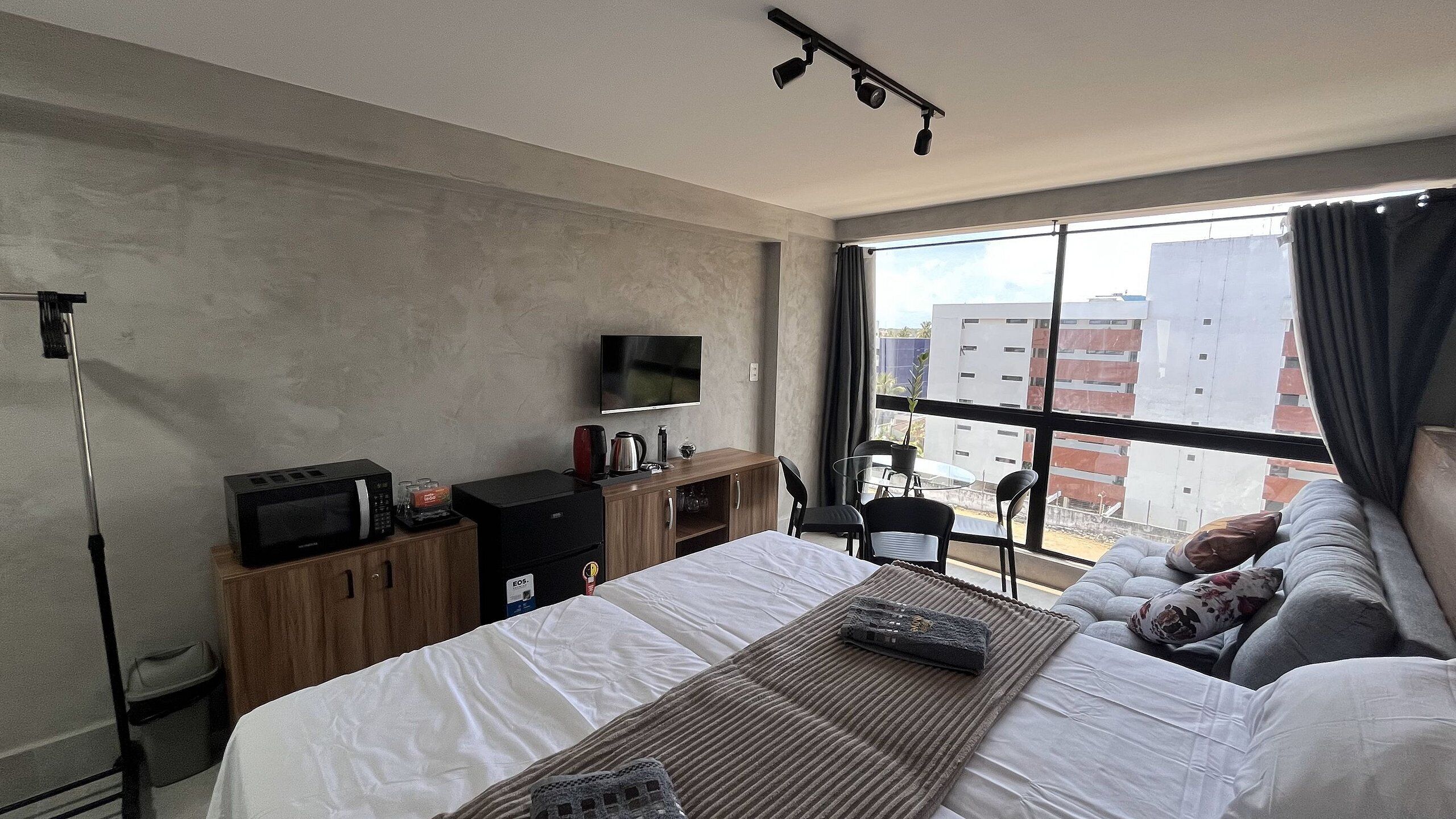 Quarto de hotel moderno com uma cama grande, uma escrivaninha com televisão de tela plana, micro-ondas e cafeteira.