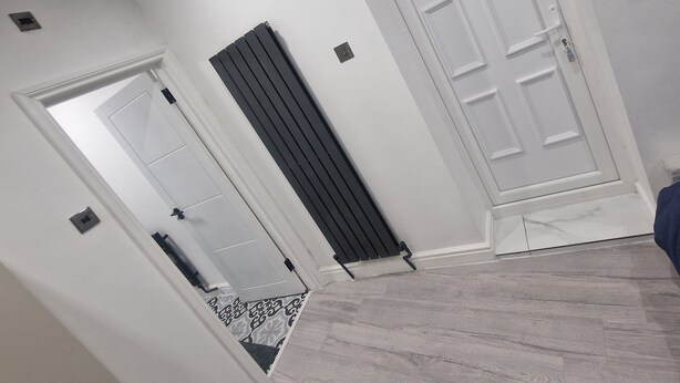 Um corredor com paredes brancas, um radiador preto e uma porta branca com design decorativo.