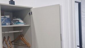 Guarda-roupa fechado com barra para pendurar e prateleira com uma caixa e uma garrafa.