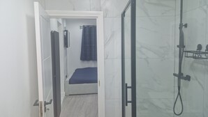 Casa de banho com chuveiro, uma cama e uma porta para outro quarto.