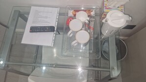 Uma mesa de vidro com uma bandeja contendo um controle remoto, um cardápio e um conjunto de xícaras de Nescafé.