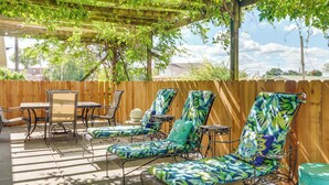 Um pátio ao ar livre com pérgola de madeira, cadeiras de metal e uma mesa.