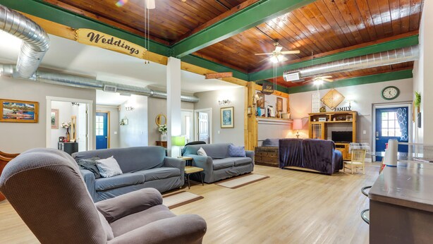 Uma sala de estar ampla com teto de madeira, um conjunto de sofás, lareira e uma placa indicando local de casamento.