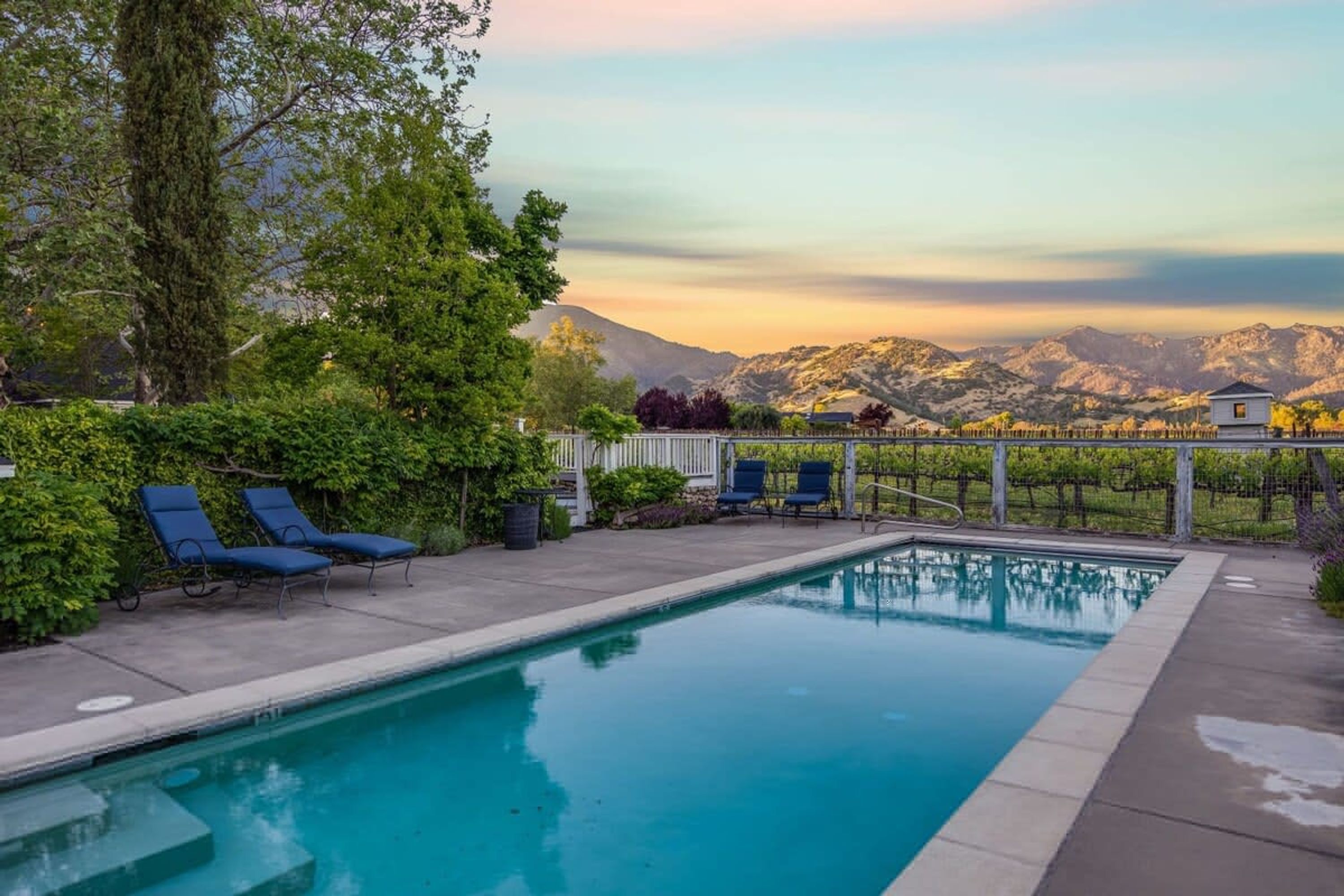 Piscina com cadeiras de sol, rodeada por vegetação e vista para a montanha.