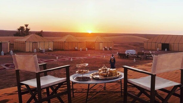 Acampamento no deserto com tendas, uma mesa de jantar com comida e cadeiras.