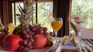 Mesa de café da manhã com frutas, um copo de suco de laranja e um pequeno vaso com flores.