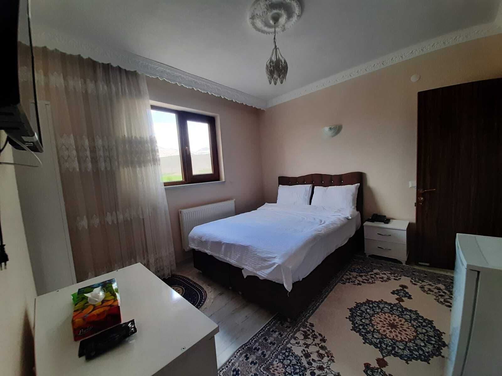 Quarto com cama, mesa de cabeceira, escrivaninha, janela e tapete estampado.