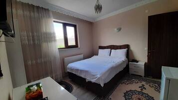 Quarto com cama, mesa de cabeceira, escrivaninha, janela e tapete estampado.