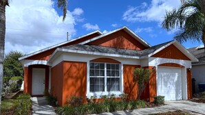 Uma casa de dois andares com fachada vermelha e branca, garagem frontal e gramado bem cuidado.