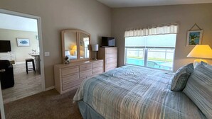 Quarto com cama, cômoda, espelho, televisão e janela com vista.