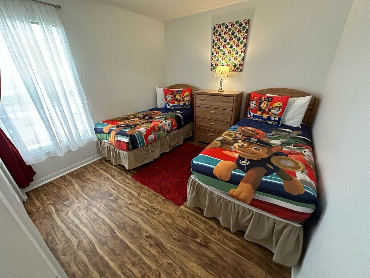 Quarto com duas camas, cômoda, tapete vermelho e um ornamento na parede.