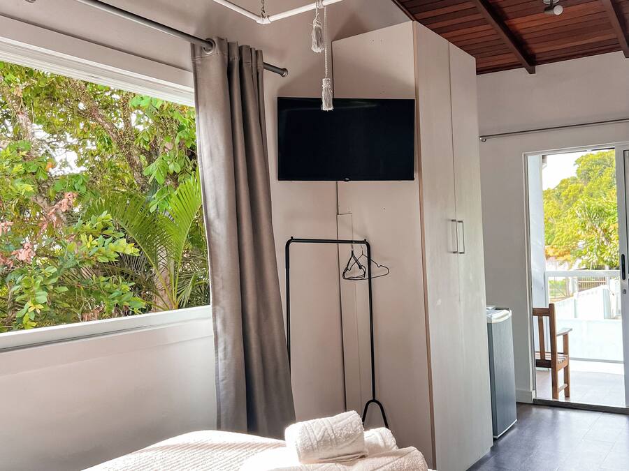 Quarto moderno com uma cama grande, uma televisão de tela plana na parede e vista para o verde lá fora.