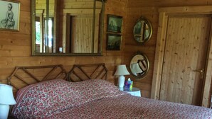 Quarto de madeira com uma cama, uma cadeira, um abajur e um espelho.