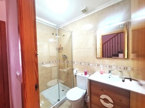 Casa de banho com chuveiro em cabine de vidro, sanita e toucador com espelho.