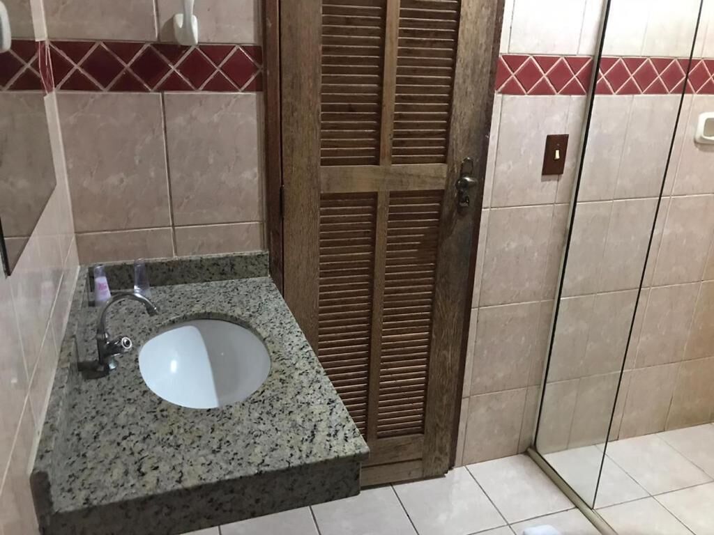 Um banheiro com pia de bancada de granito, porta de madeira com painéis venezianos e paredes revestidas com padrão em vermelho e bege.