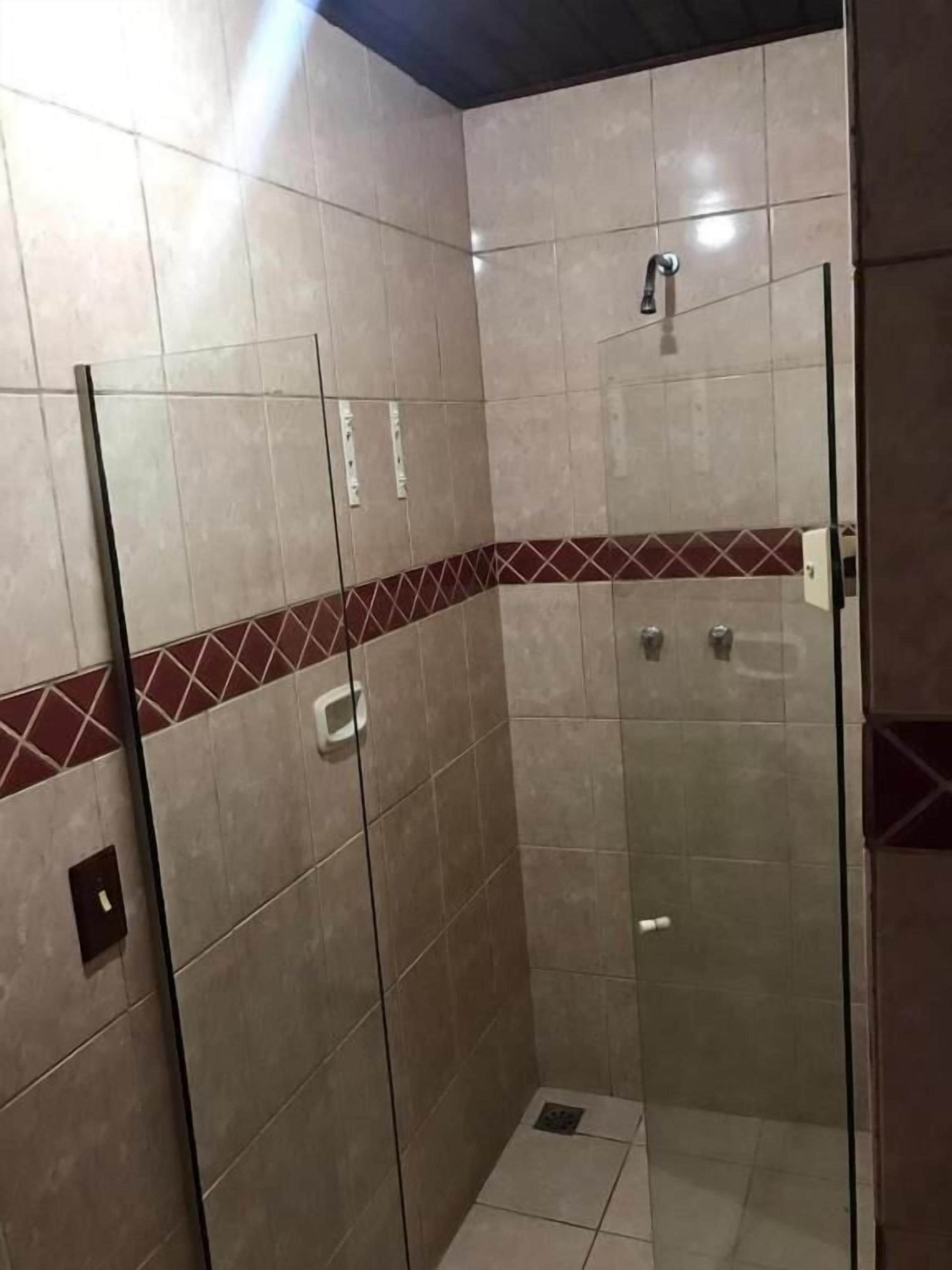 Box de chuveiro com paredes de vidro, azulejos bege e uma faixa decorativa em azulejos vermelhos.