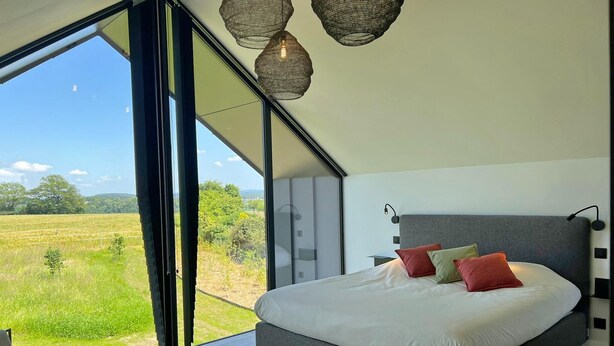 Um quarto com uma cama grande, vista para um campo verde e teto inclinado.
