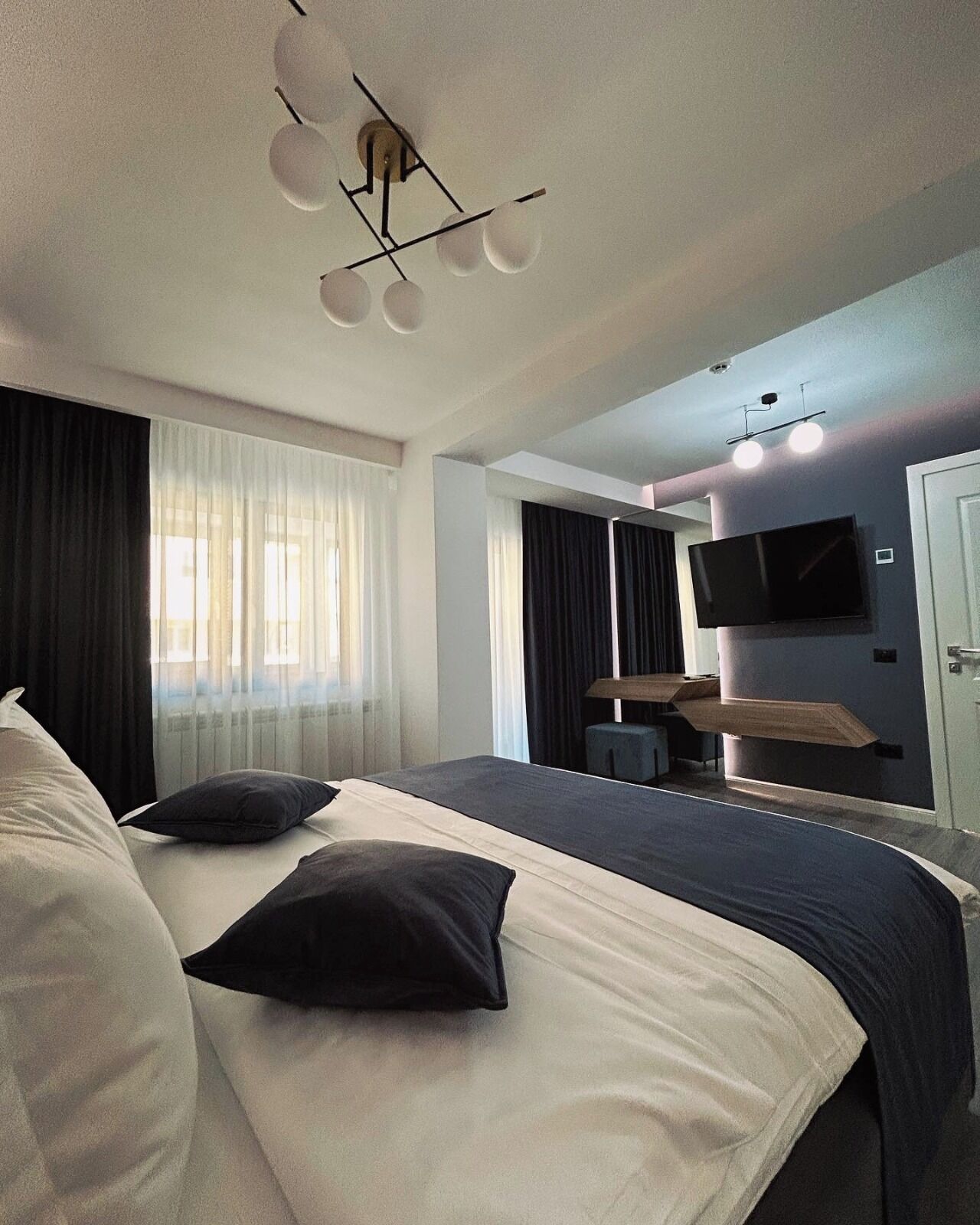 Quarto de hotel moderno com uma cama grande, televisão de tela plana na parede e luminária no teto.