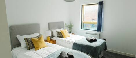 Quarto de hotel com duas camas, uma janela com cortinas, um radiador e um lustre.