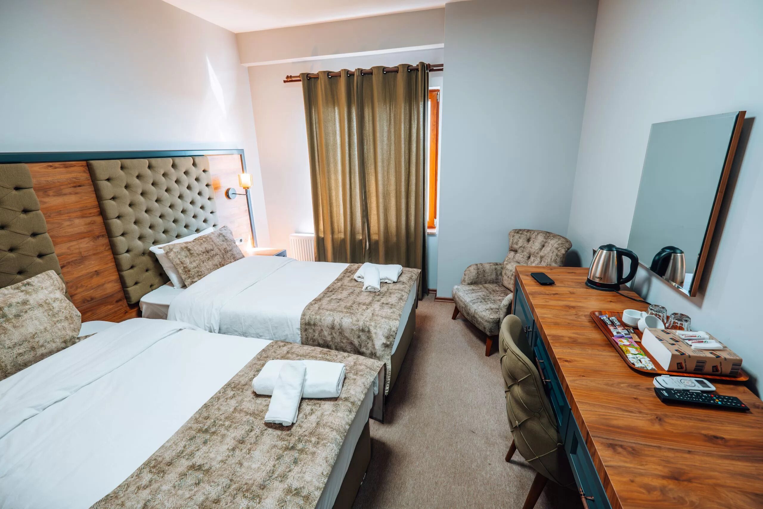 Quarto de hotel com duas camas, uma escrivaninha de madeira, uma cadeira, cafeteira e um espelho.